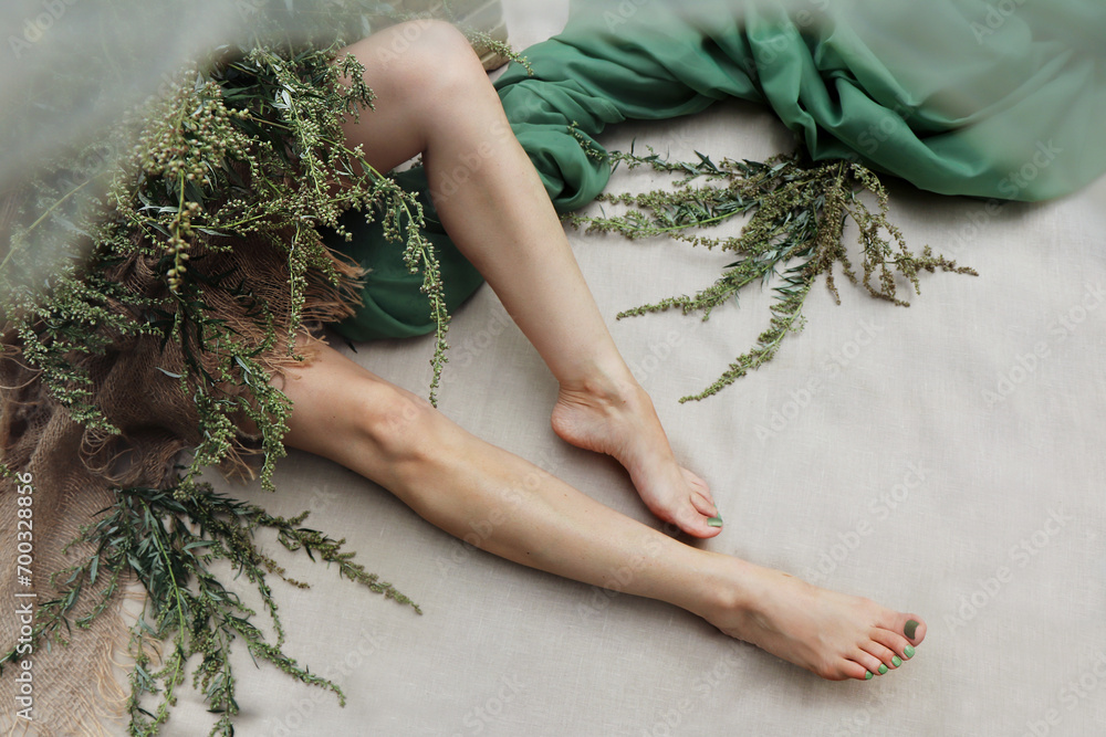 Women's legs with a green pedicure on a linen background with plants ...