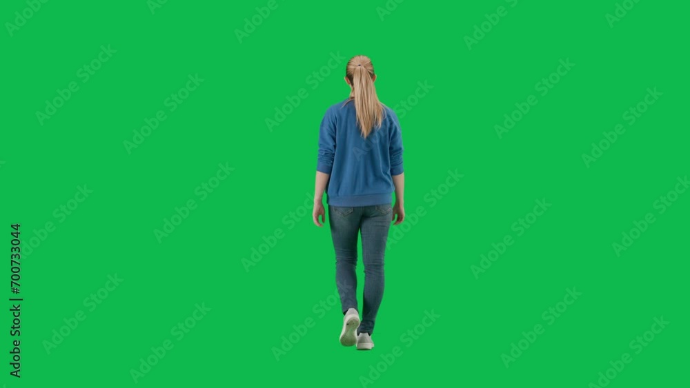 Back view of a young woman in full height walking on a green screen. A ...