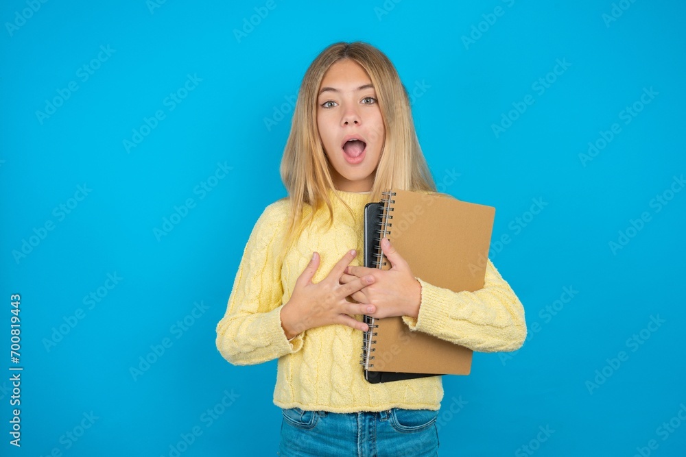 Scared Beautiful kid girl wearing yellow sweater holding notebook looks ...