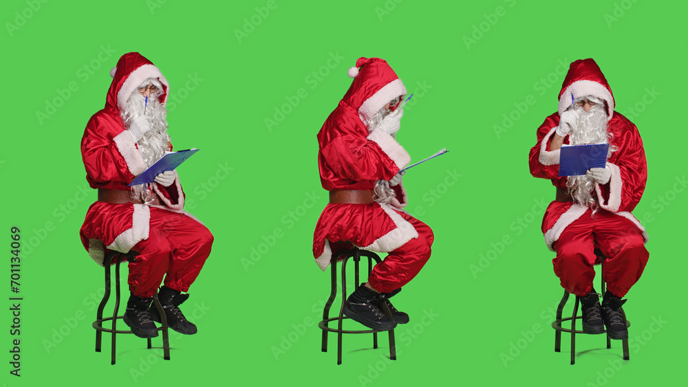 Saint nick writing notes on clipboard while he sits on chair dressed in ...