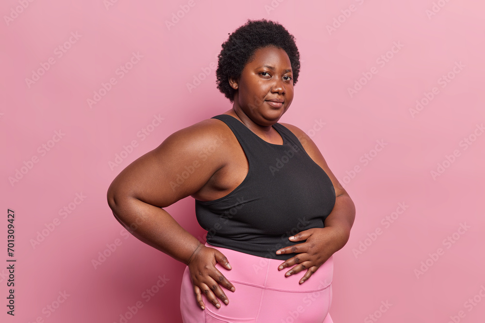 Sideways shot of curly haired African woman keeps hands on stomach and ...