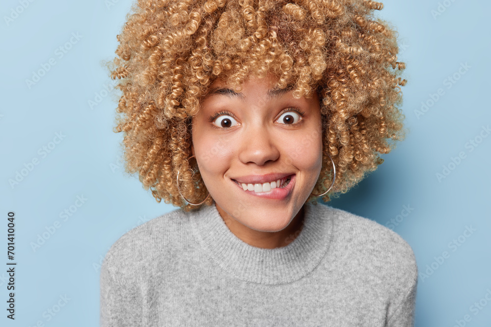 Portrait Of Surprised Curly Haired Woman Bites Lips And Stares With