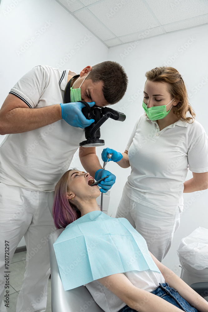 male dentist takes a photo of his client's teeth during an appointment ...