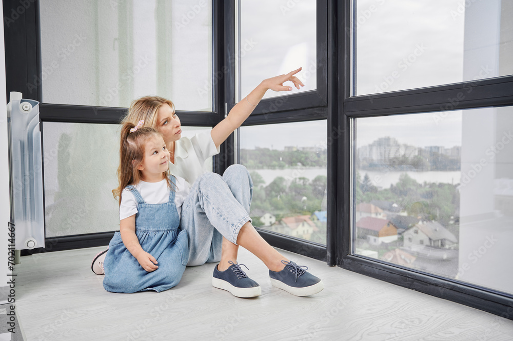 Woman and little girl sitting on the floor and looking and pointing out ...