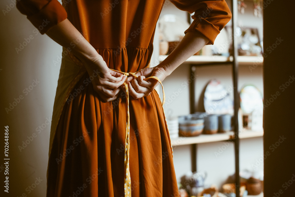 Woman's hands tying an apron, rear view. A potter prepares for work by ...