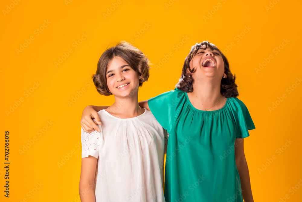 Portrait of two smiling sisters over yellow background. Choldhood and ...