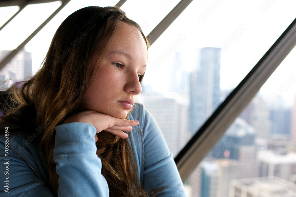 a young girl sits by the window, sad, lifts her chin with her hand ...