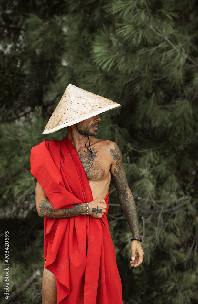 Sexy male monk in red cape and an Asian triangular hat with tattoos in ...