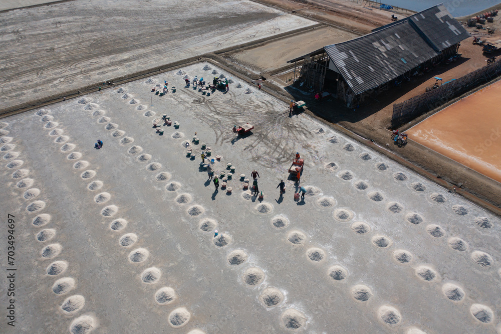 Aerial top view of farmers making heaps of raw sea salt piles with sea ...
