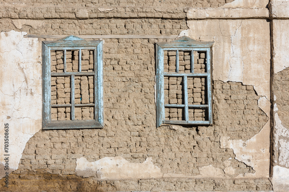 old house adobe air brick wall with two embedded wooden window frames ...