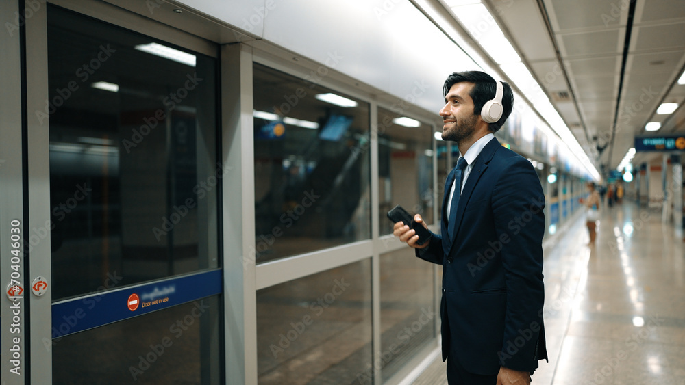 Project manager wearing headphone at train station while holding mobile ...