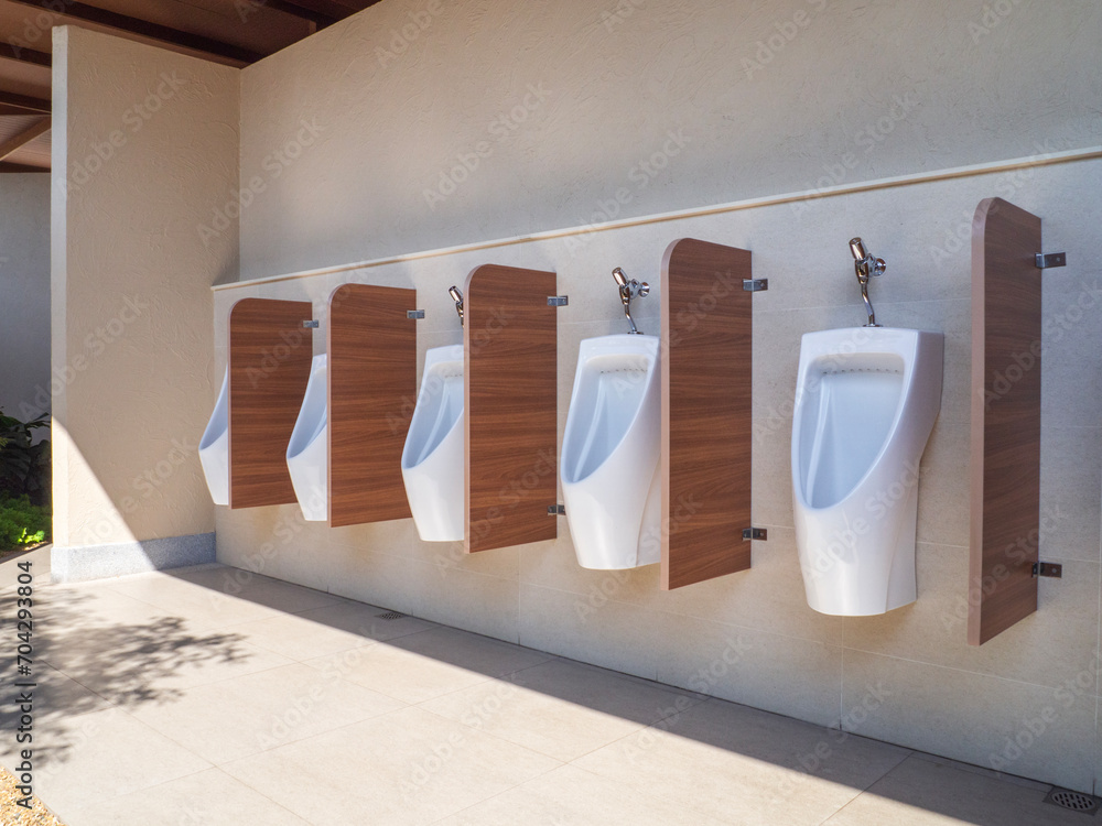 modern clean public restroom with tiles. Line of men's white urinals in ...