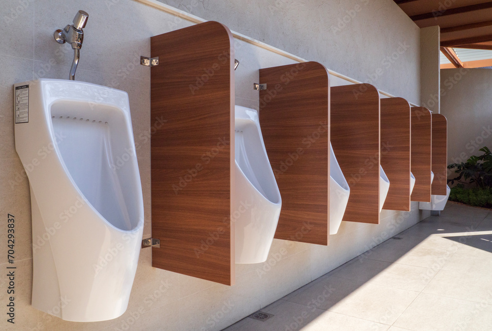 modern clean public restroom with tiles. Line of men's white urinals in ...