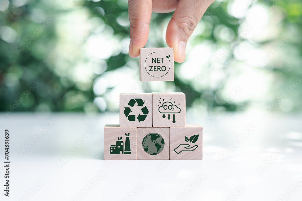 Hand put wooden cubes with green net zero icon and green icon on bokeh ...