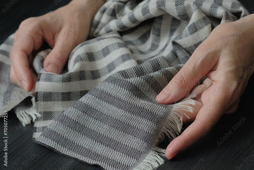 Women's hands unfold a gray scarf on the dark surface of the table ...