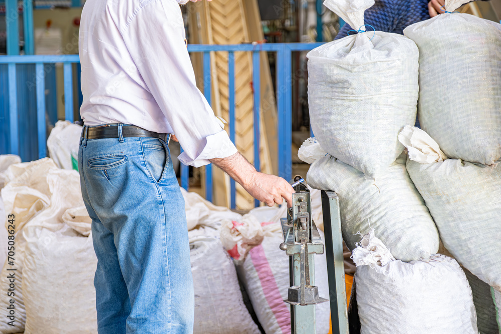 Employee and employer weighing sacks of olives using old style scale ...
