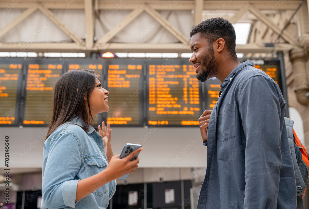 Group of multiracial friends checking time on departure board at a ...