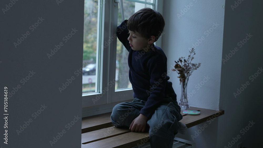 Child seated by apartment window looking out at view from home with ...