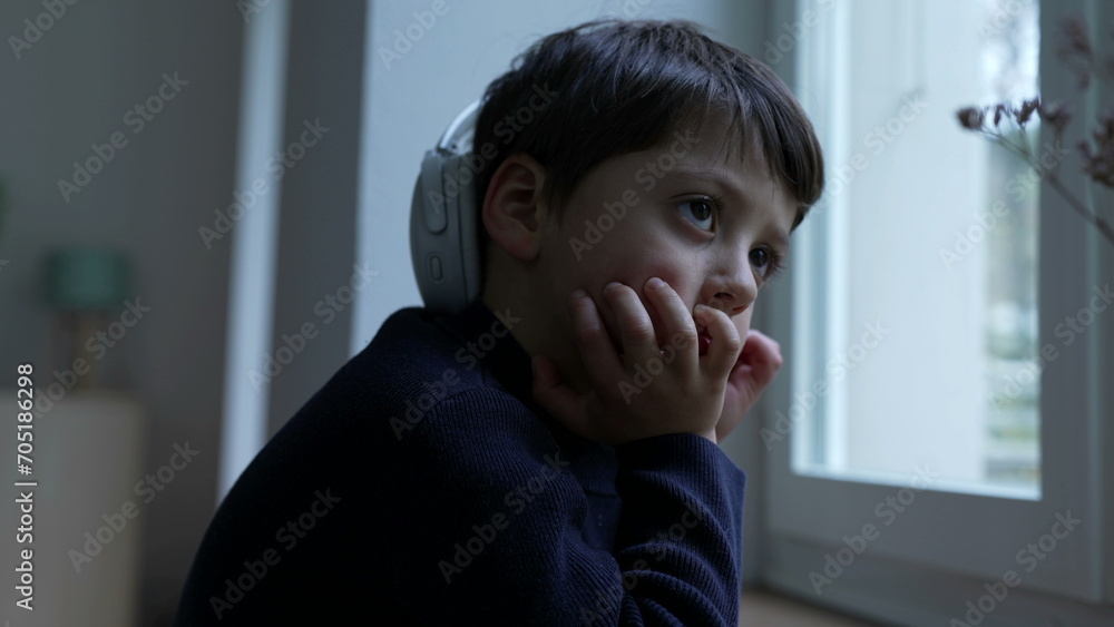 Thoughtful small boy with hand in chin daydreaming at home by window ...