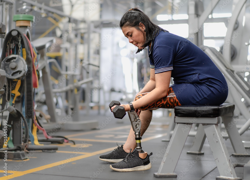 Woman with prosthetic leg sitting in gym lifting dumbbell weight ...