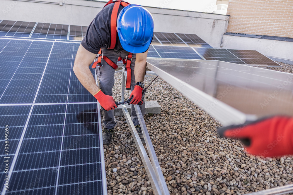 Solar panel technician with drill installing solar panels on roof. technician installing ...