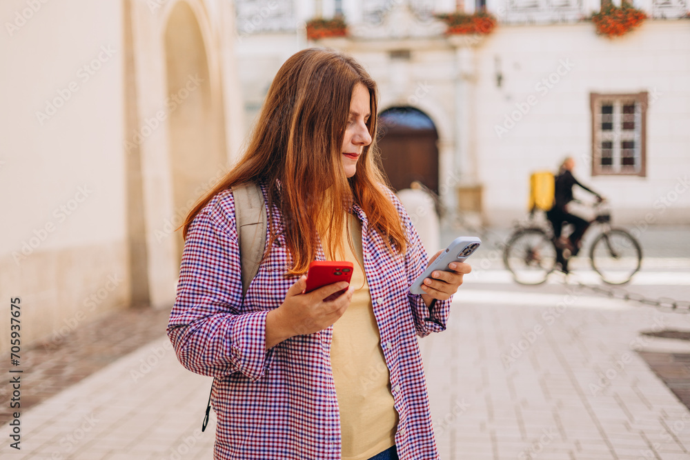 Sad angry girl in shirt with two phones standing on city street ...