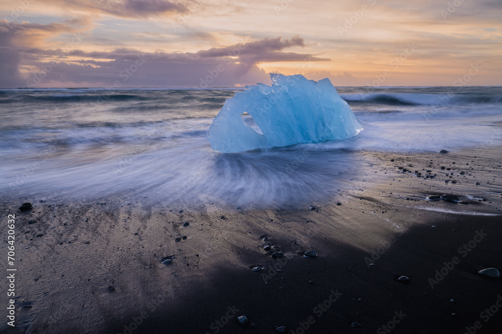 Wave washing around a blue ice fragment at Diamond black sand beach in ...