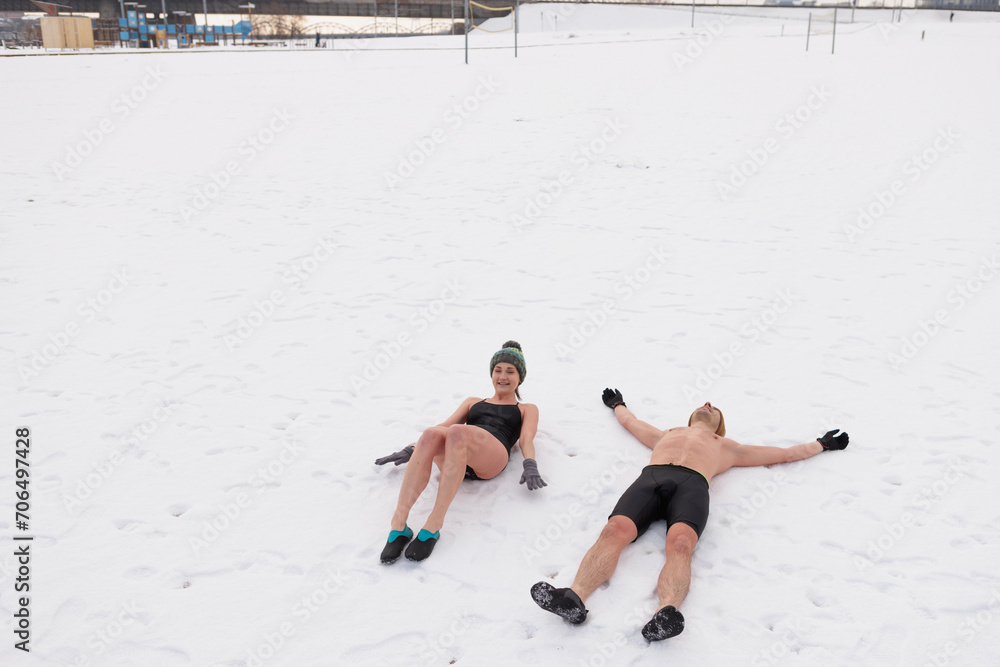 People laying in the snow wearing swimsuit. Young couple after winter ...