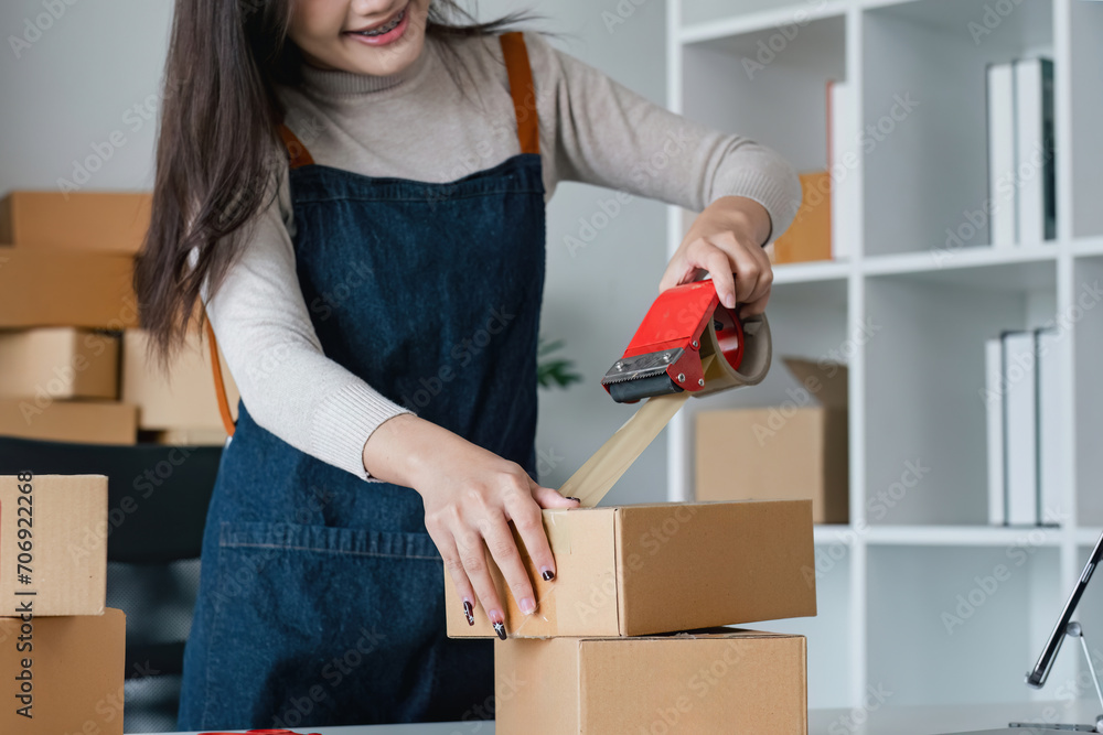 Young asian woman taping up a cardboard box in home office SME e ...