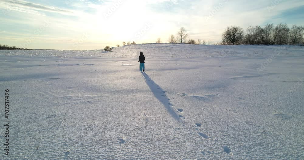 A human with trekking poles walks through a snowdrift on a frosty ...