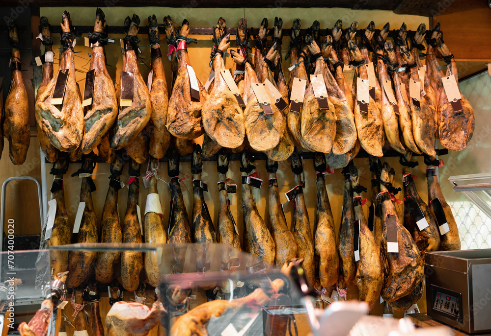 Row of dangling legs jamon with labels on showcase of butcher shop ...