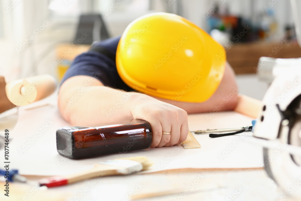 Arm of drunken worker in yellow helmet hold liquor bottle portrait ...