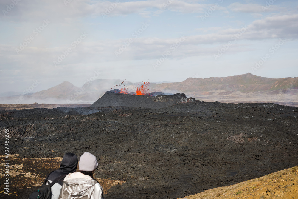 Woman tourist looking at dramatic view of dark volcanic landscape with ...