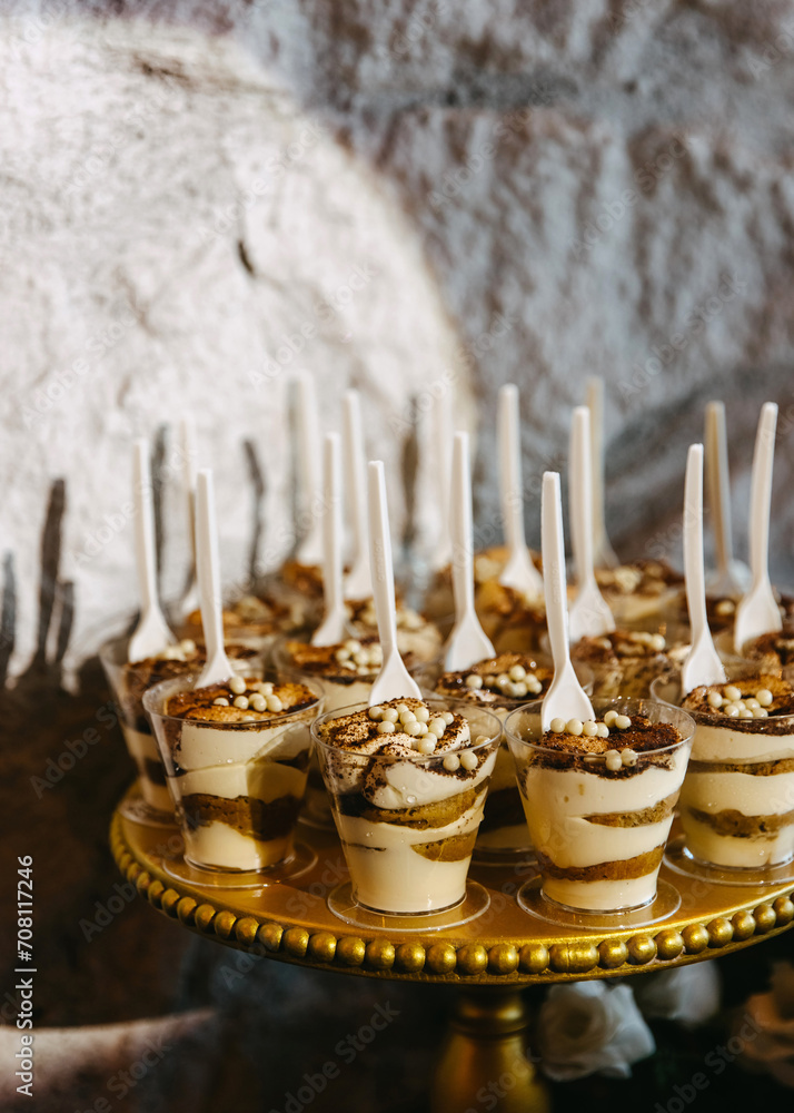 Small plastic cups with tiramisu desert on a golden stand in sun light ...