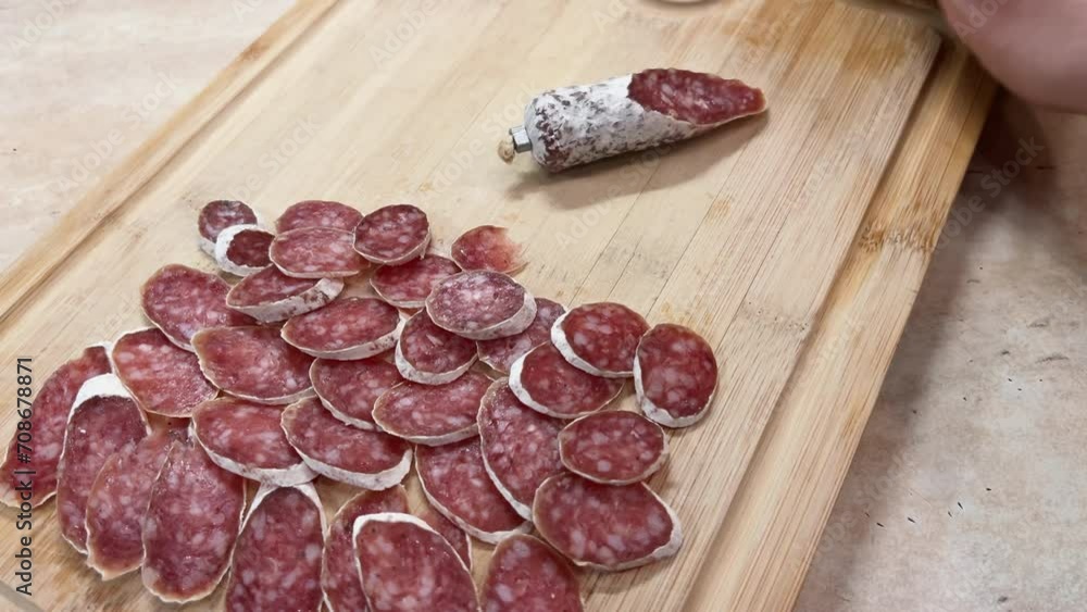 Hands rotating wooden cutting board with slices of fuet sausage with ...