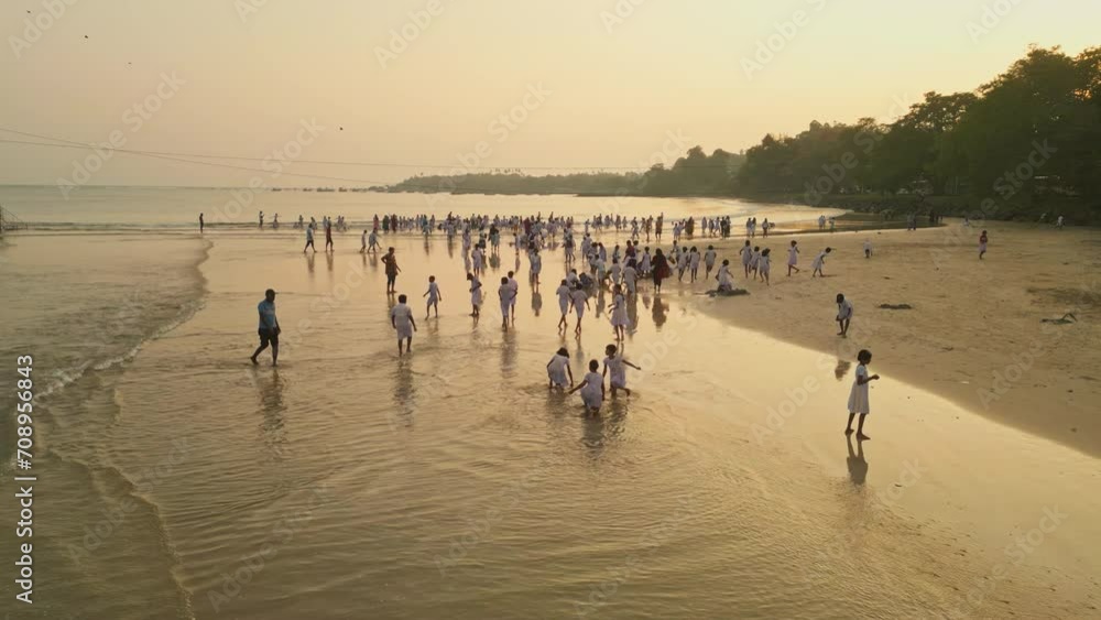 Children in white uniforms play joyfully on sandy beach as waves lap at ...
