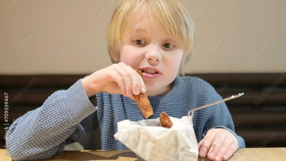 Cute blonde preteen boy eating chicken nuggets or wings with sauce at ...