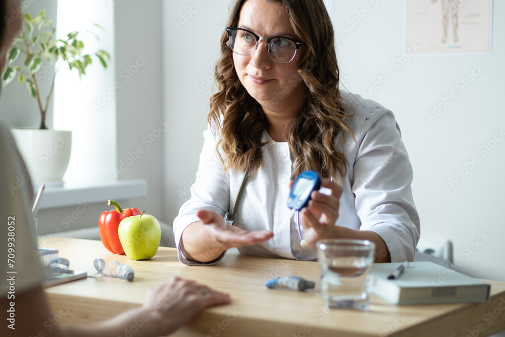 The doctor shows the glucometer to the patient. A female ...