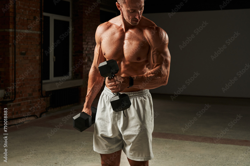 A muscular athlete stands with dumbbells in his hands. His torso looks ...