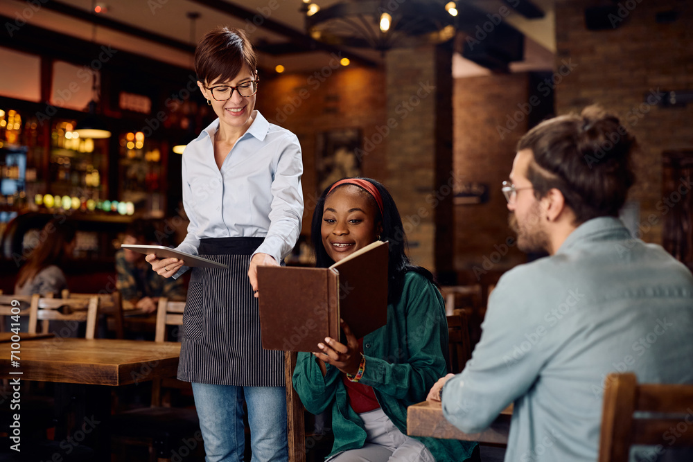 Happy waitress recommending order from menu to her customers in pub ...