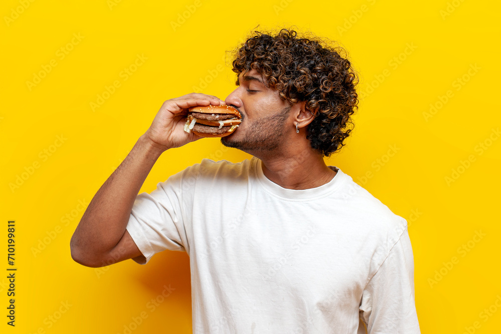 young hungry indian guy eating delicious cheeseburger on yellow ...