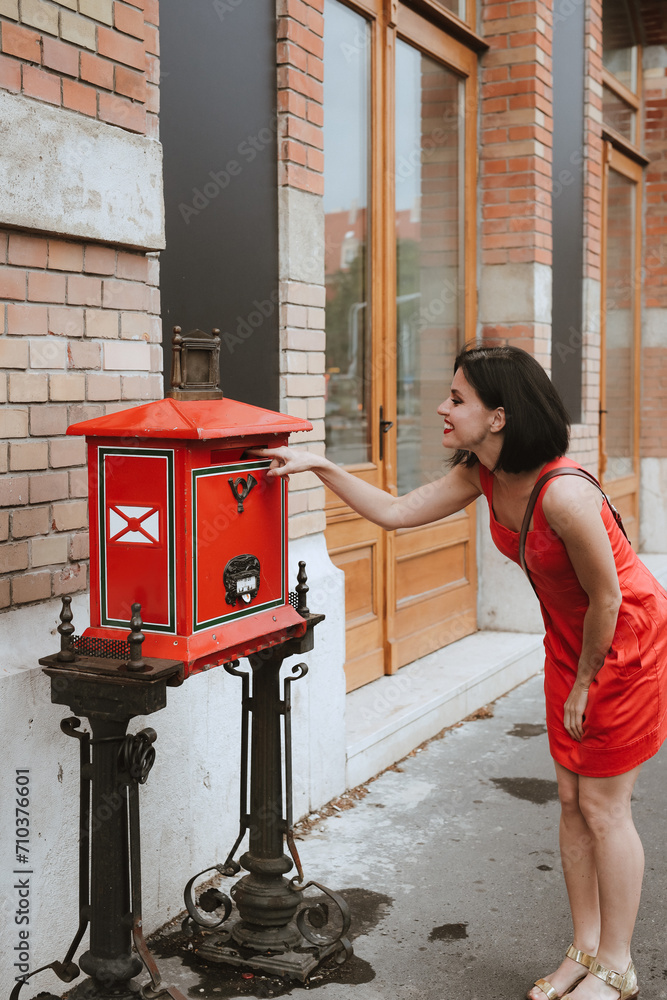 A woman looks into a red street mailbox. The girl throws a letter into ...