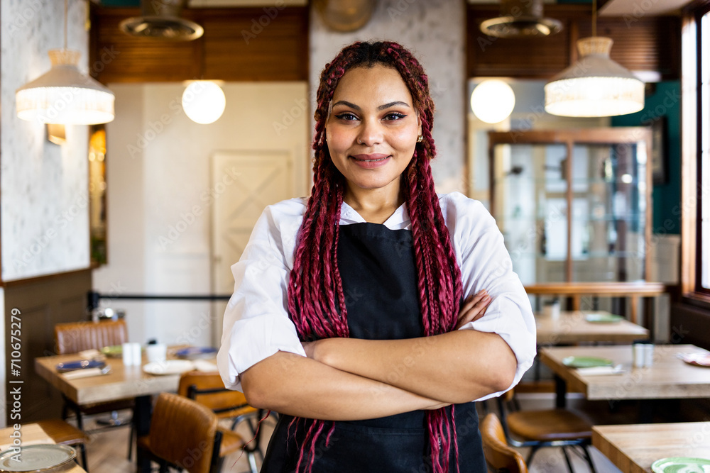 A dark-skinned woman in a waitress uniform poses happily with her arms ...