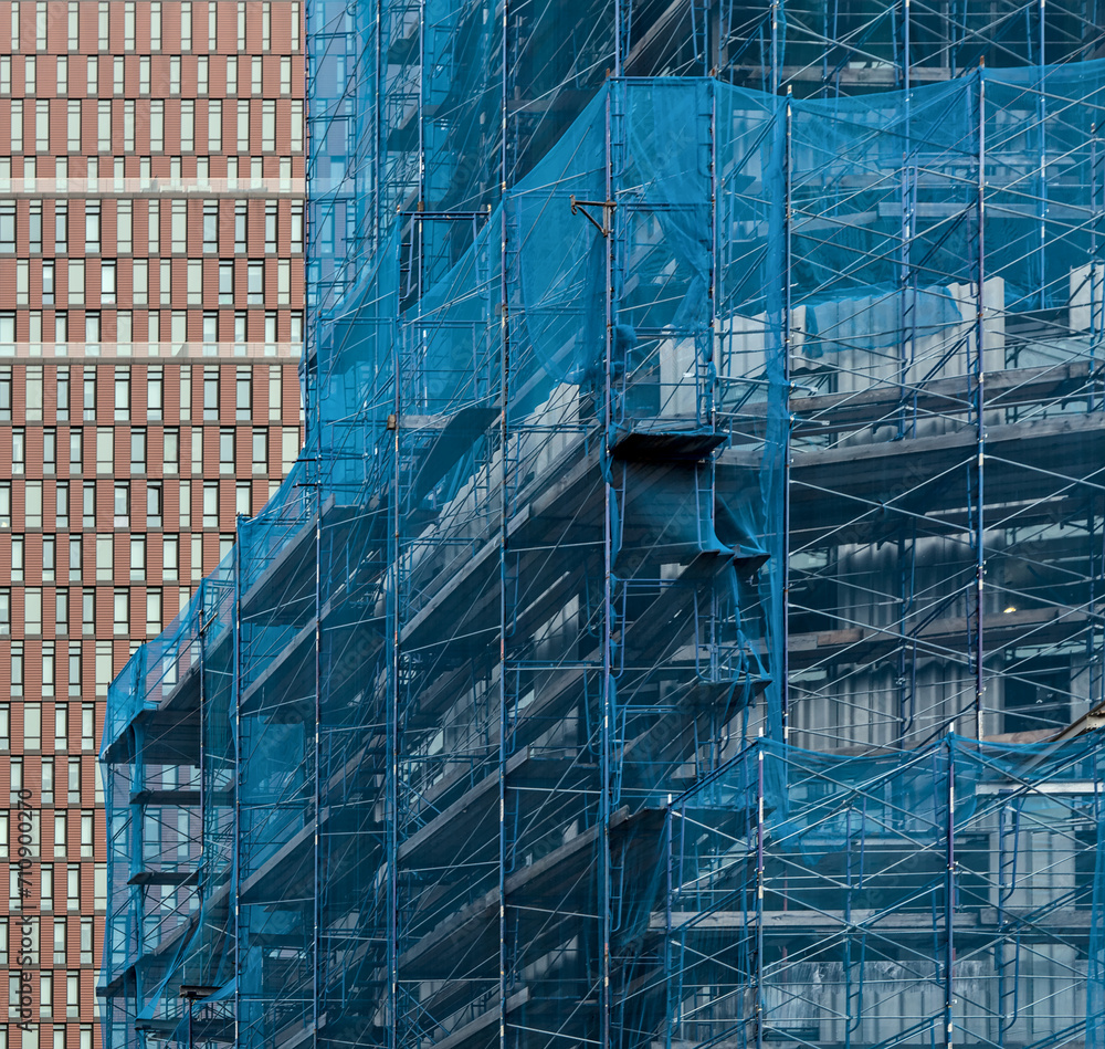 building under construction covered in blue mesh tarp protective wrap ...