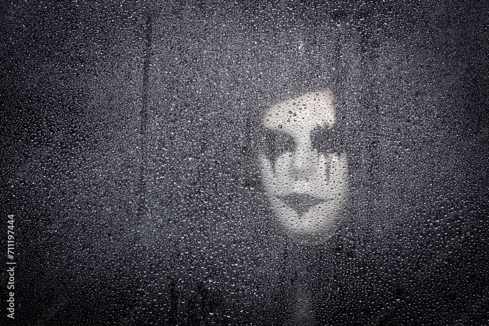 Creepy horror mask with cloak with raindrops on window glass Stock ...
