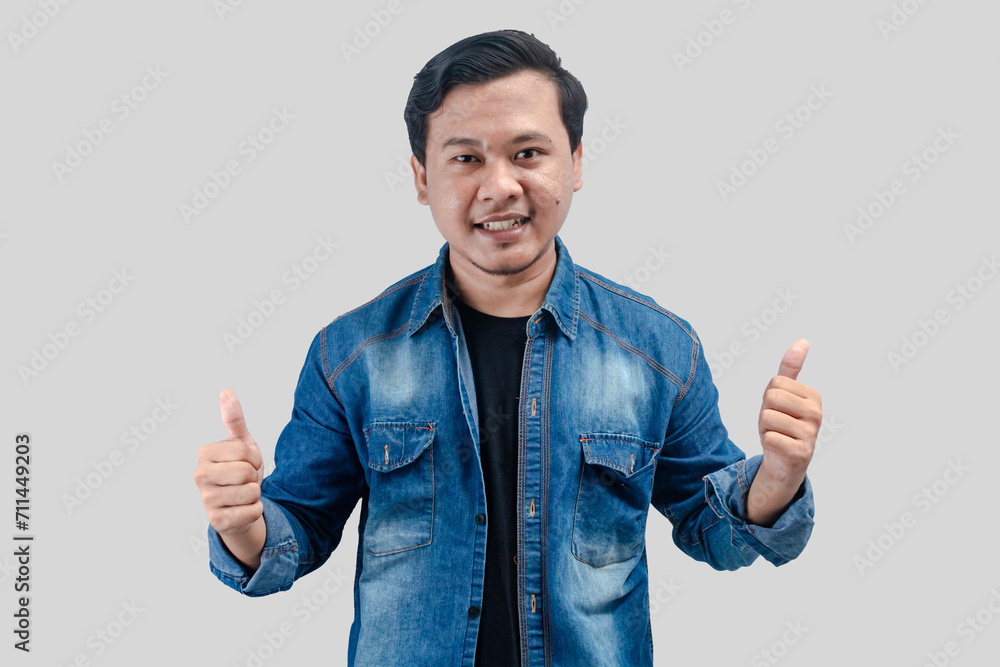Young Asian Man showing thumb up in approval, recommending, like smth good, standing over white ...