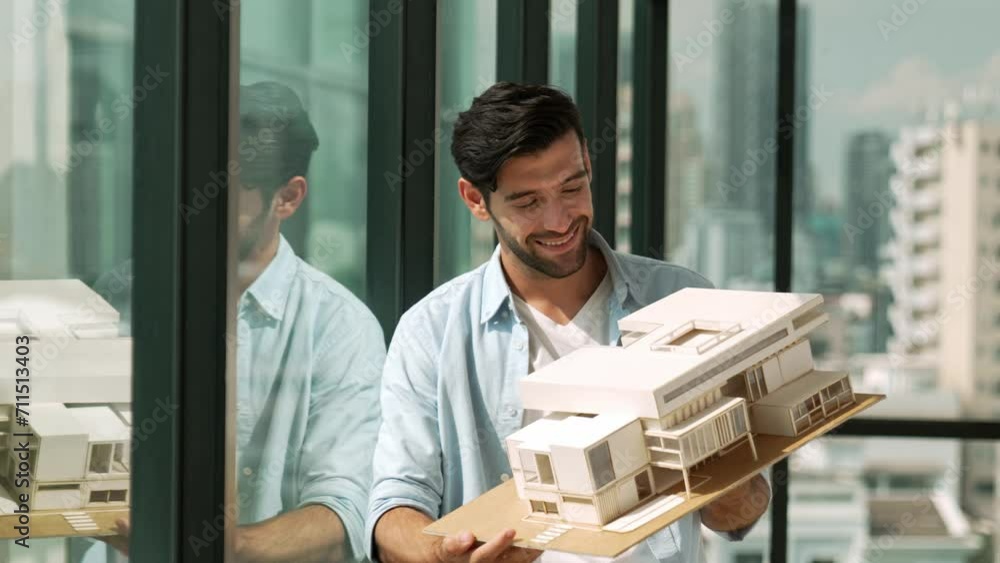 Skilled smiling caucasian engineer turns house model left and right to ...