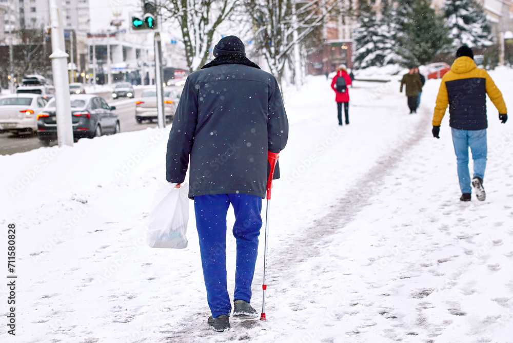 Foto de Disabled senior man walks with crutches during snowfall. Lame ...
