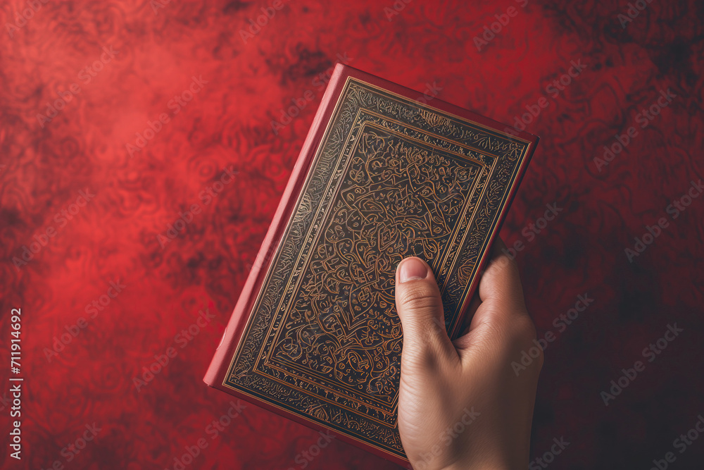 Hand Clasping A Richly Decorated Quran Against a Deep Red Background in ...