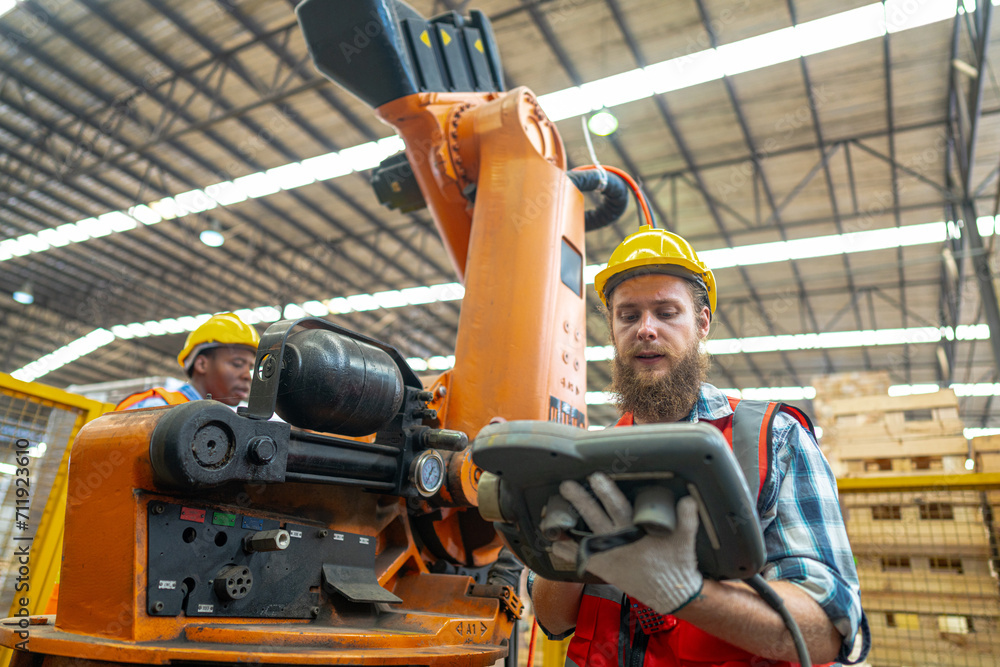 Engineer standing by robotic arm and operating machine in factory ...